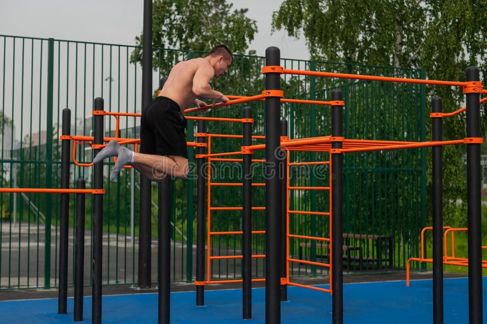 A Shirtless Man is Doing a Workout on the Horizontal Bars Outdoors ...
