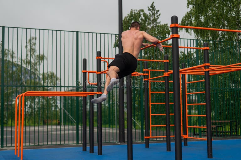 A Shirtless Man is Doing a Workout on the Horizontal Bars Outdoors ...