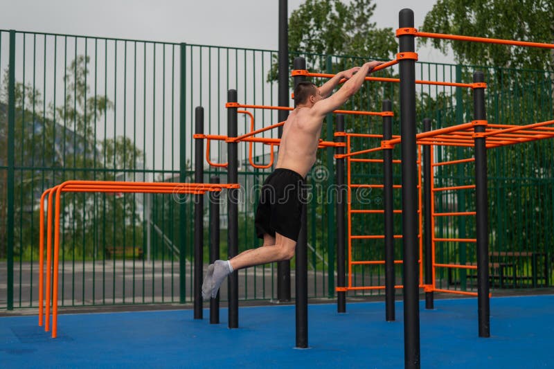 A Shirtless Man is Doing a Workout on the Horizontal Bars Outdoors ...