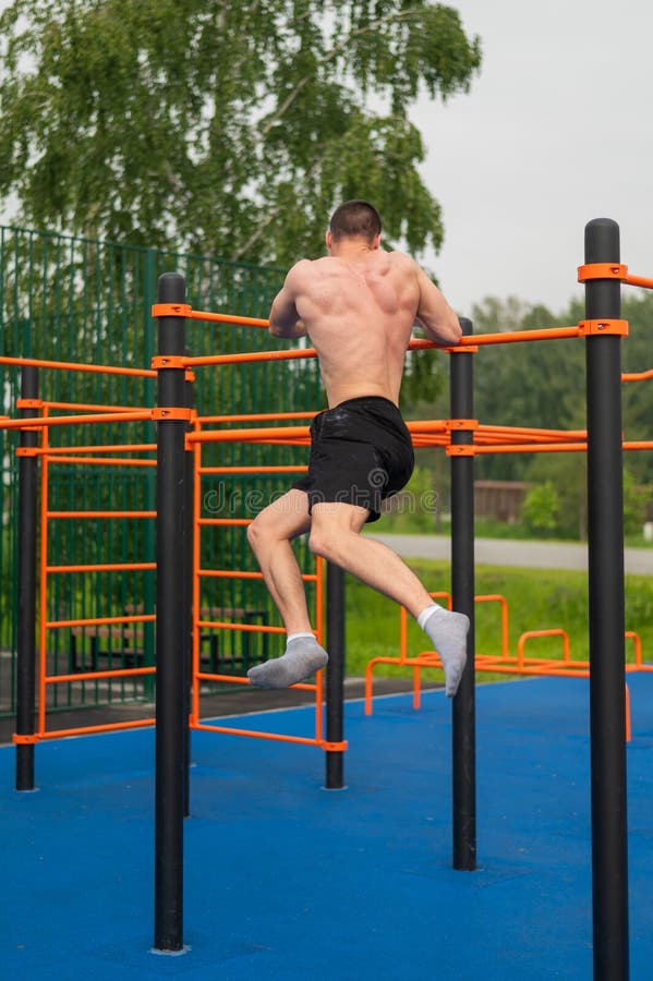 A Shirtless Man is Doing a Workout on the Horizontal Bars Outdoors ...