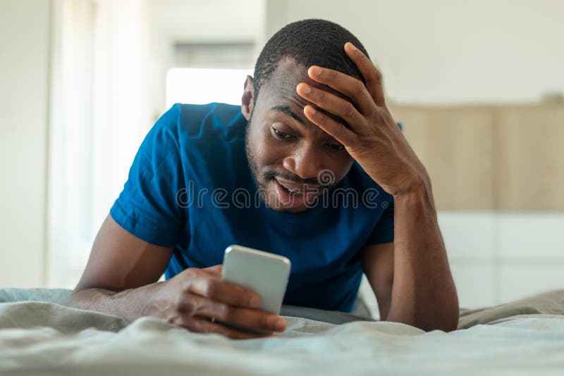 Shocked Black Man Texting on Phone Lying in Bedroom Stock Photo - Image ...