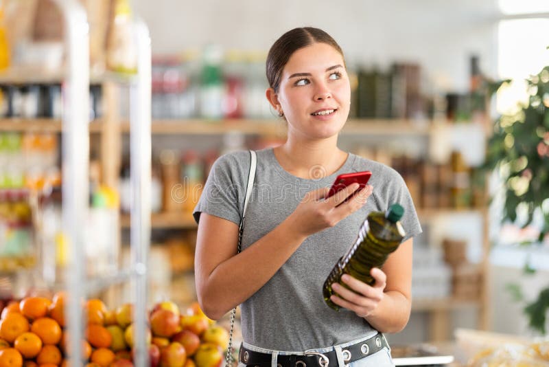 In Shop Youth Girl Scan QR Code and Take Reading Olive Oil Package Bottle Using Phone Camera ...