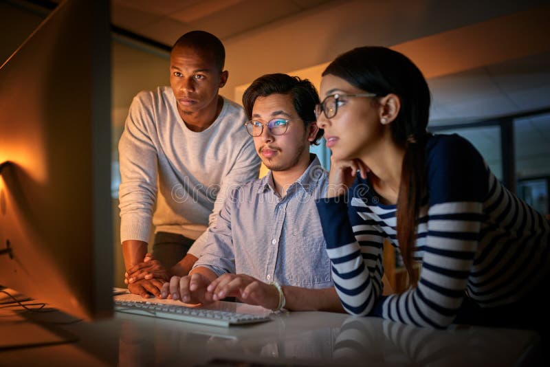 Getting Work Done Together. Shot of Computer Programmers Working Together Late in the Office ...