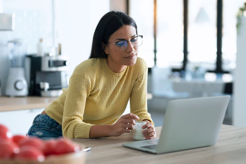 Confident Young Woman Working with Computer while Eating Yogurt Sitting ...