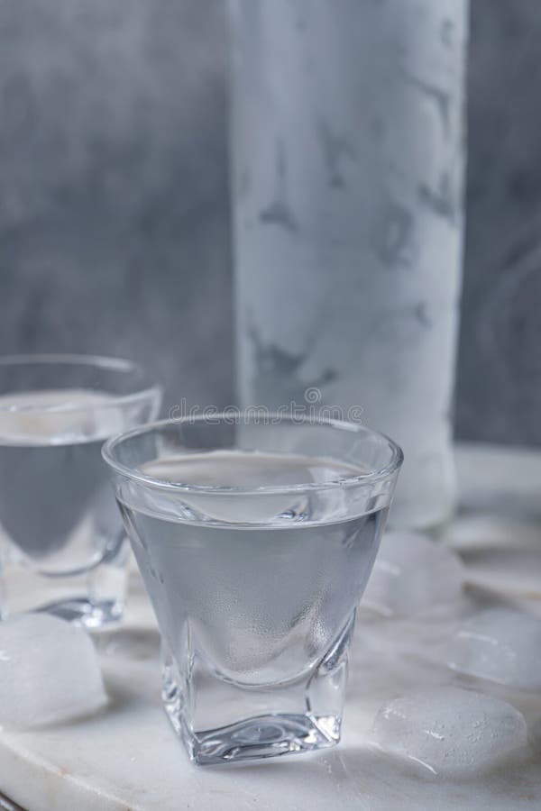 Shot Glasses and Bottle of Vodka with Ice Cubes on Table Stock Photo ...