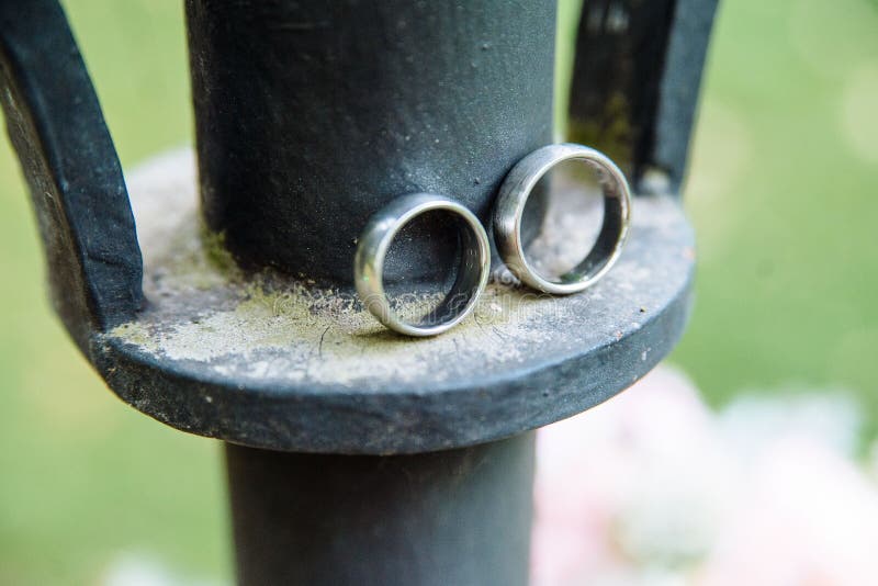 Two Silver Wedding Rings Rest on a Textured Metal Surface, Symbolizing ...