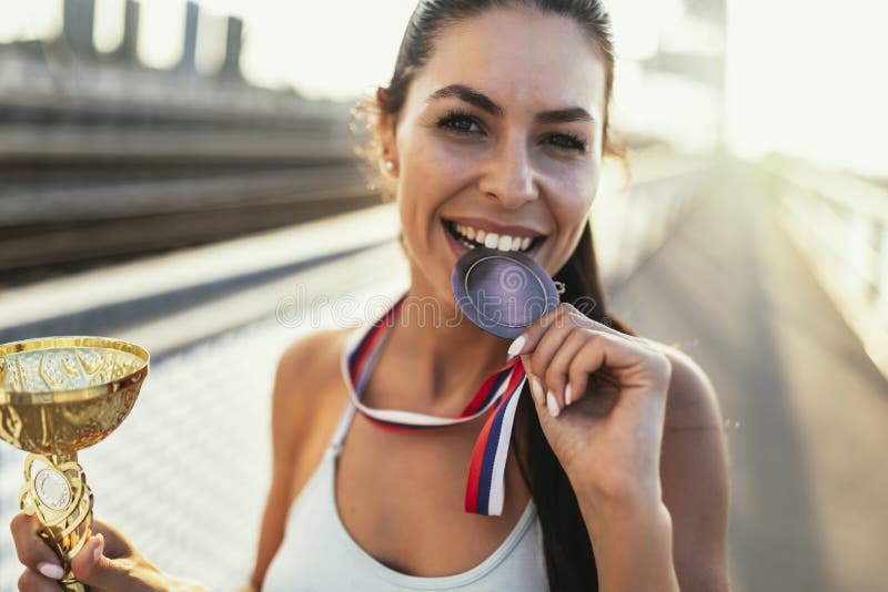 Young Female Athlete Holding Cup while Biting Her Medal Stock Photo ... Young Female Athlete Holding Cup while Biting Her Medal Stock Photo ...