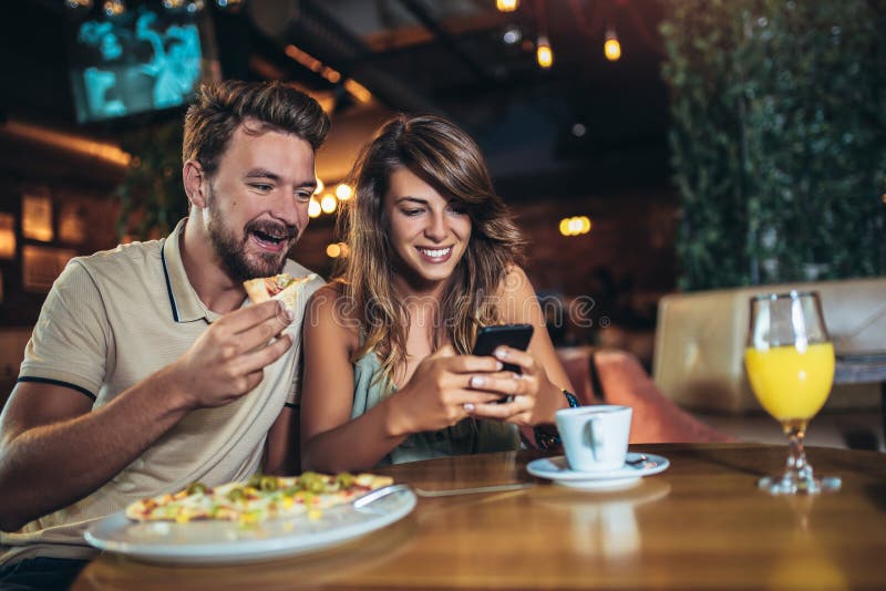 Young Happy Couple Using Phone and Eating Pizza in a Restaurant ...