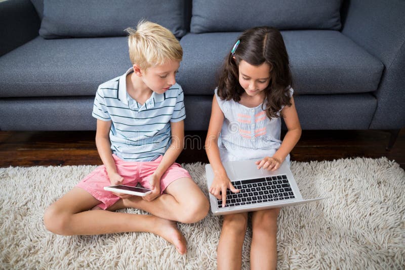 Siblings Using Digital Tablet and Laptop in Living Room Stock Image ...