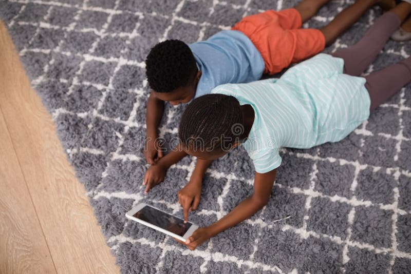 Siblings Using Digital Tablet while Lying on Rug at Home Stock Image ...
