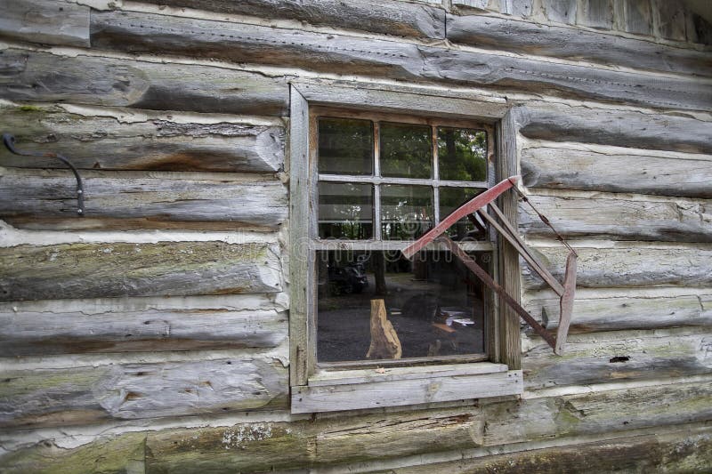Side Facade of a Log Farmhouse and Window with Old Saw Hanging in ...