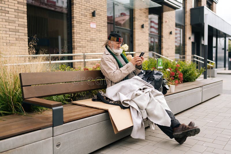 Side View of Aged Homeless Man Sitting on Urban Bench, Using Smartphone ...