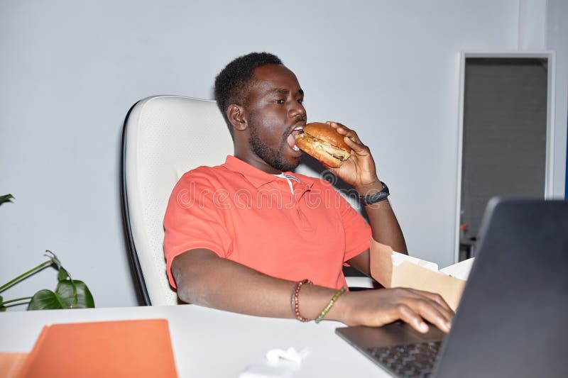 Black Man Eating Burger at Workplace Indoors Stock Photo - Image of ...