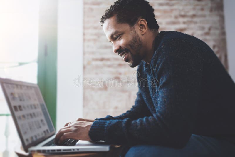 Cheerful African Man Using Computer and Smiling while Sitting on the ...