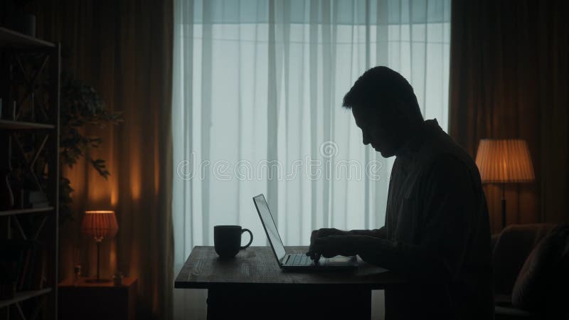 Side View of a Dark Silhouette of a Man at a Table in Front of a Laptop ...