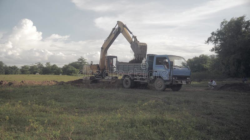 Side View of an Excavator Loading Earth Inside a Small Truck in Open ...