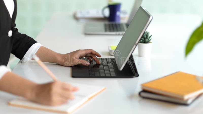 Female Hand Writing on Notebook and Typing on Tablet Keyboard on Office ...