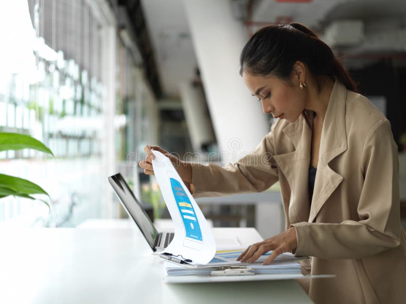 Female Office Worker Reading Document File while Working with Laptop on ...