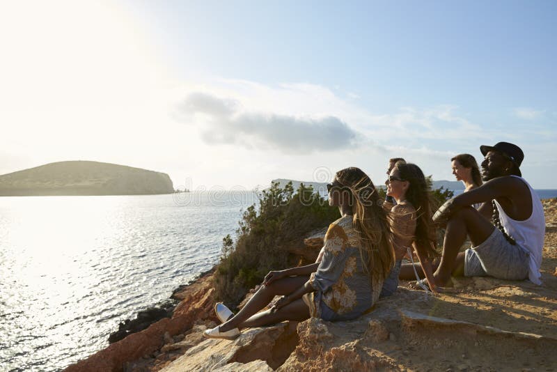Side View of Friends Sitting on Cliff Watching Sunset Stock Image ...