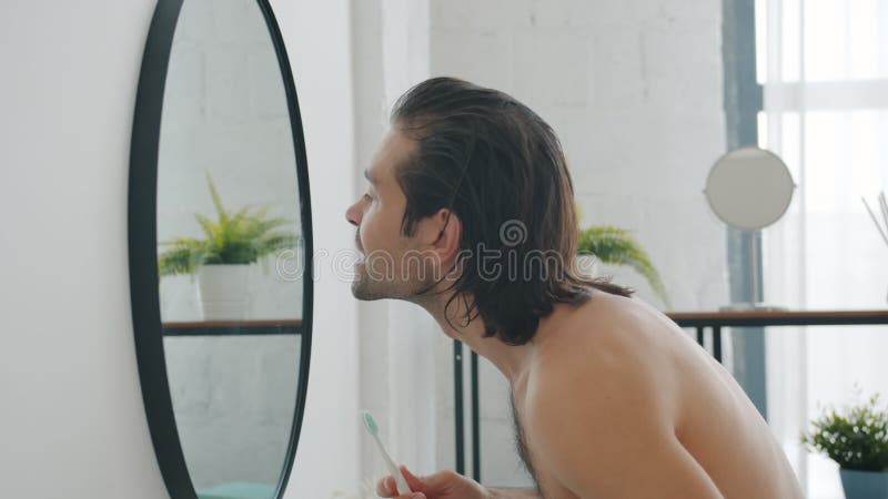 Side View of Guy Brushing Teeth and Looking at Mirror on Bathroom Wall ...