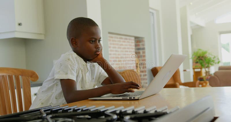 Side View of Little Black Boy Using Laptop at Dining Table in a ...