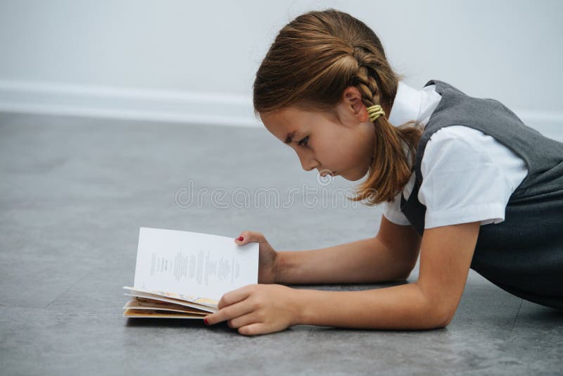 Side View of a Little Schoolgirl Lying on the Floor, Reading a Textbook ...