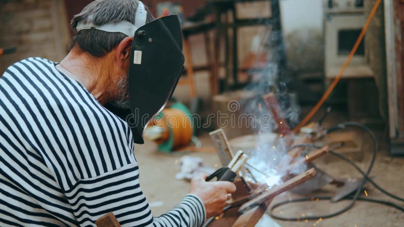 Side View of Person in a Welding Helmet Welds Metal Products on the ...
