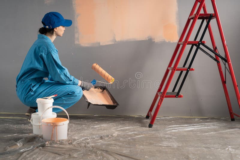 Side View of Painter with Cap Squatting Ready Painting a Wall with ...