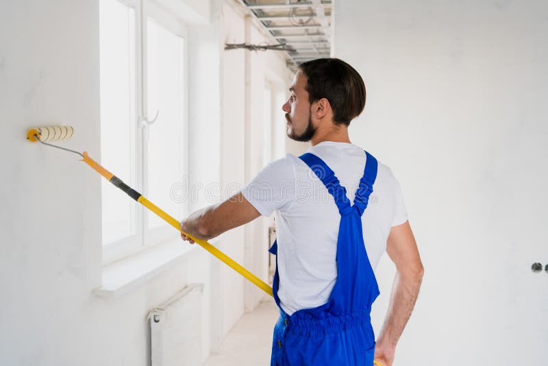 Side View of a Painter Painting a Corridor Wall White with a Roller ...