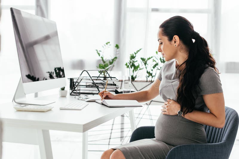 View of Pregnant Woman Sitting Behind Table with Computer, Keyboard and ...