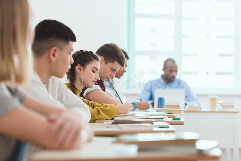 Side View of Schoolchildren Sitting in Row and Teacher at Table with ...
