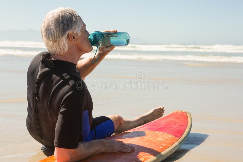 Side View of Senior Man Drinking Water while Sitting on Surfboard Stock ...