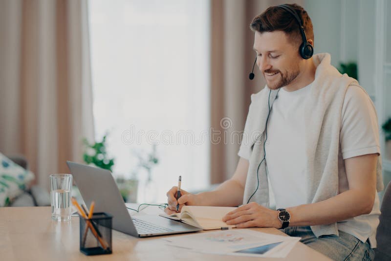 Happy Young Man Sitting at the Table at Home and Making Notes in Note ...