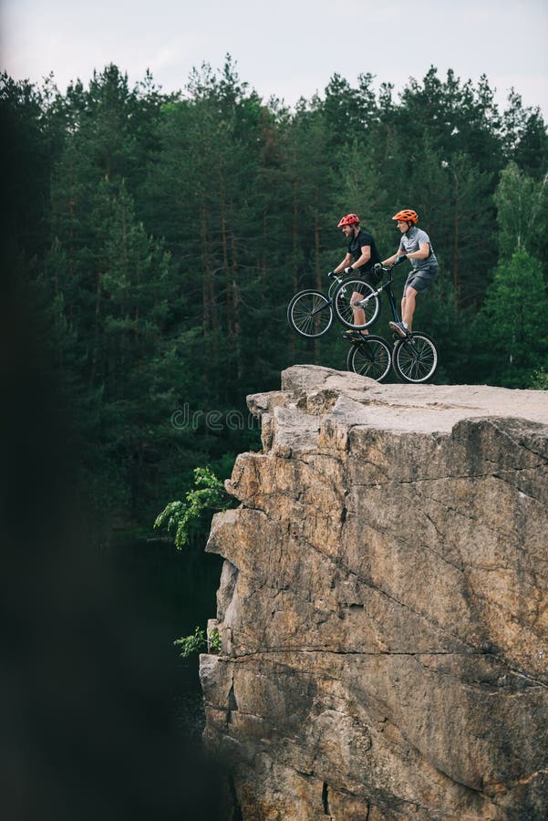 Side View of Trial Bikers Standing on Back Wheels on Rocky Cliff with ...