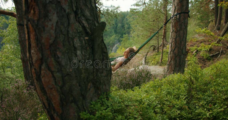 Side View of a Woman Resting in a Hammock with Backdrop of Trees and ...