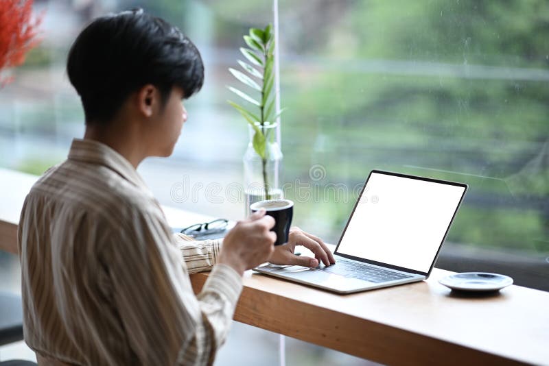Young Man Holding Coffee Cup and Working with Laptop Computer in Cafe ...
