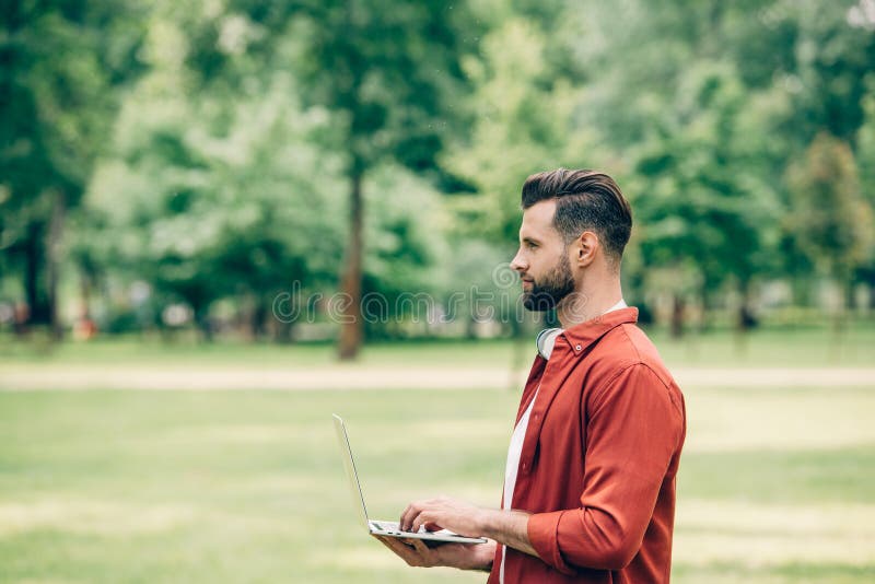 View of Young Man Standing in Park with Laptop in Hands and Looking ...