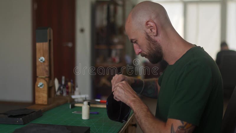 Side View of Young Professional Leather Craftsman Sits at Work Table ...