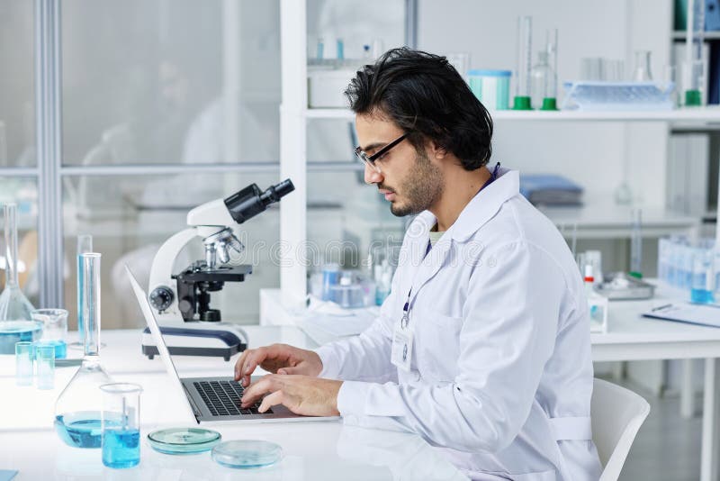 Side View of Young Serious Laboratory Worker in Labcoat Sitting in ...