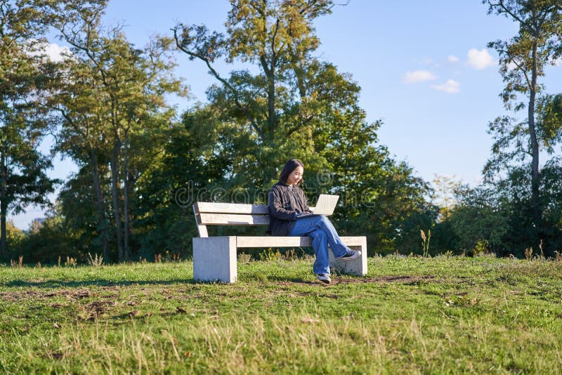 Side View of Young Woman Sitting Alone in Park on Bench, Using Her ...