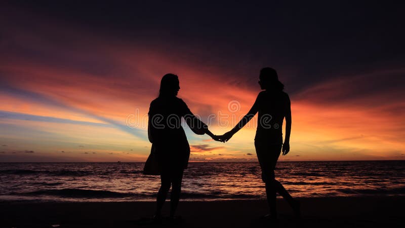 Silhouette De Deux Filles Tenant Des Mains Ensemble Sur La Plage Image