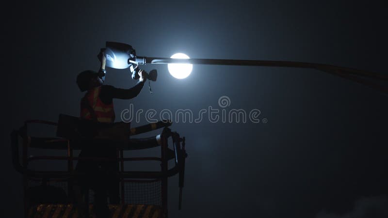 Silhouette of a Electric Engineer Working on a Street Lamp with the ...