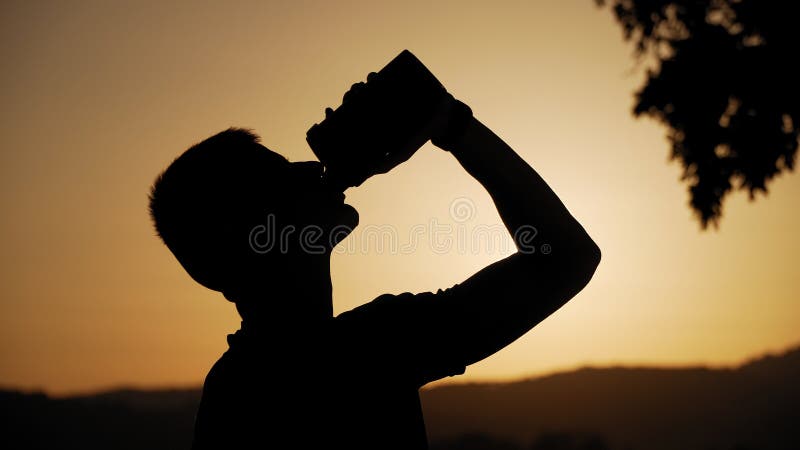Silhouette of Fit Young Man Drinking Water with Sun Behind it in Sunset ...