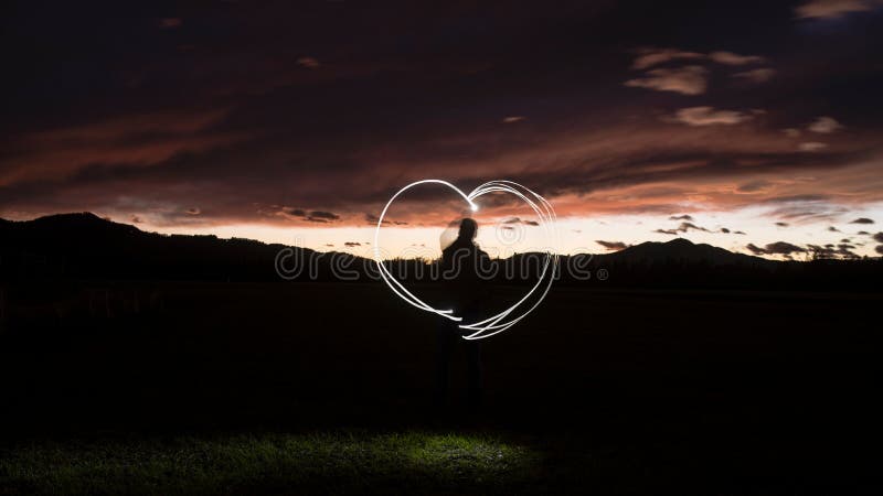 Silhouette of a Man Draws a Heart Shape with a Flashlight through the ...