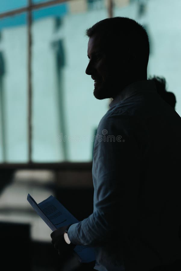 Silhouette of Man Holding Paperwork Walking, Looking at Something and ...