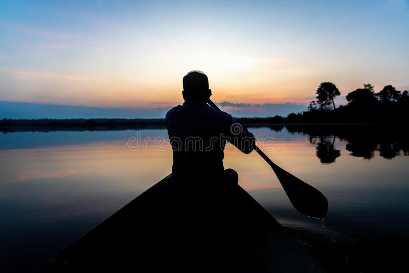 Silhouette of a Man Paddling Canoe at Dusk Calm Water Stock Photo ...