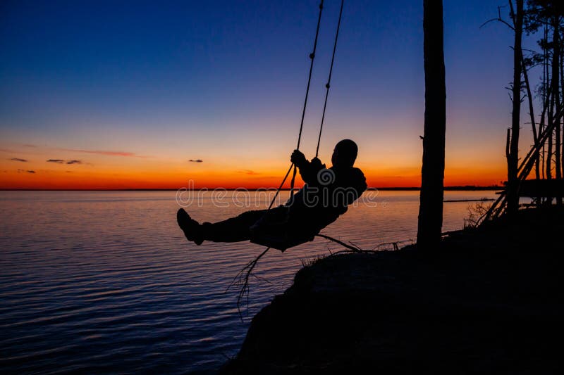 Silhouette of Man on Rope Swing Above River at Sunset Stock Image ...