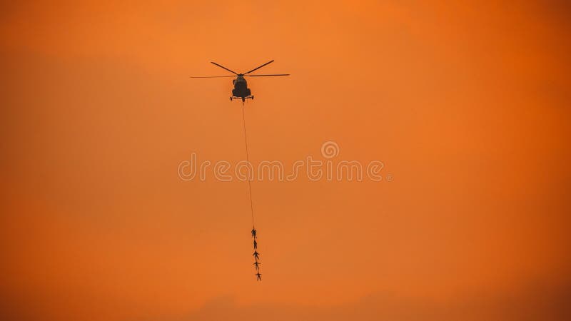 Silhouette of People Hanging from a Helicopter on a Rope in the Air ...