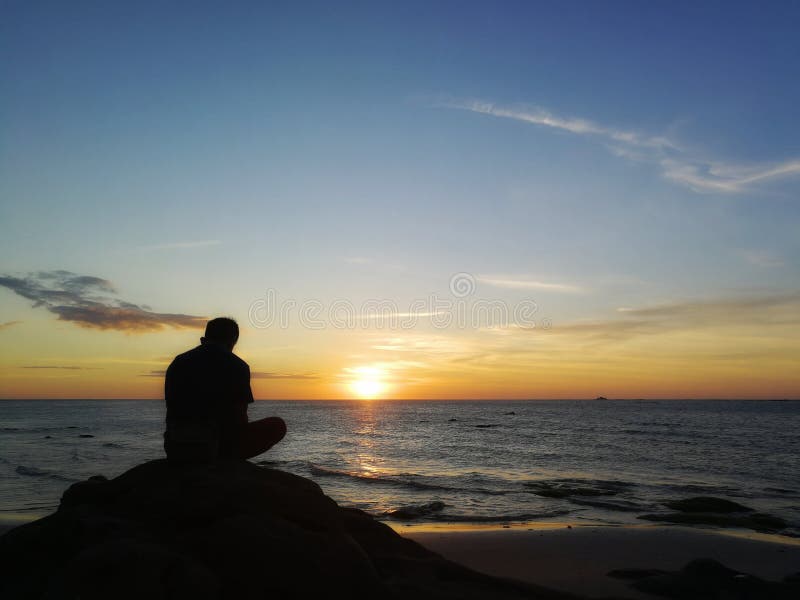 Silhouette of Young Man Sitting on the Rock while Watching the Sunset ...