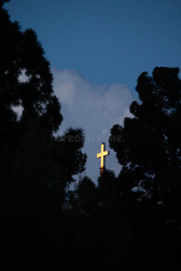 Silhouetted Trees Surrounding a Glowing White Cross on a Blue Sky with ...